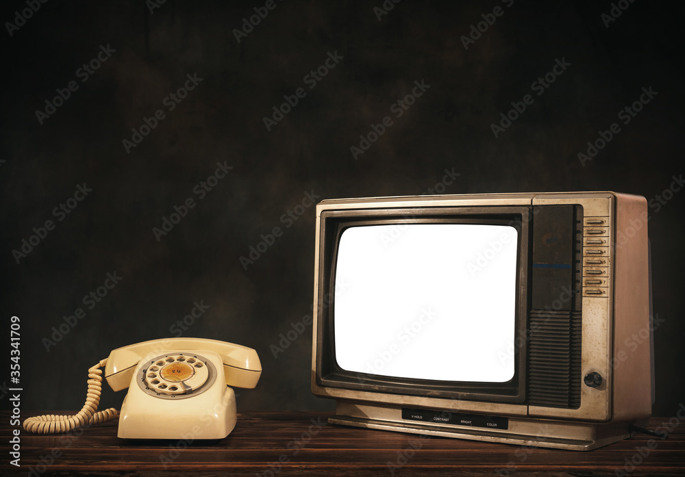 Retro old television and old telephone on wood table with dark wall ...