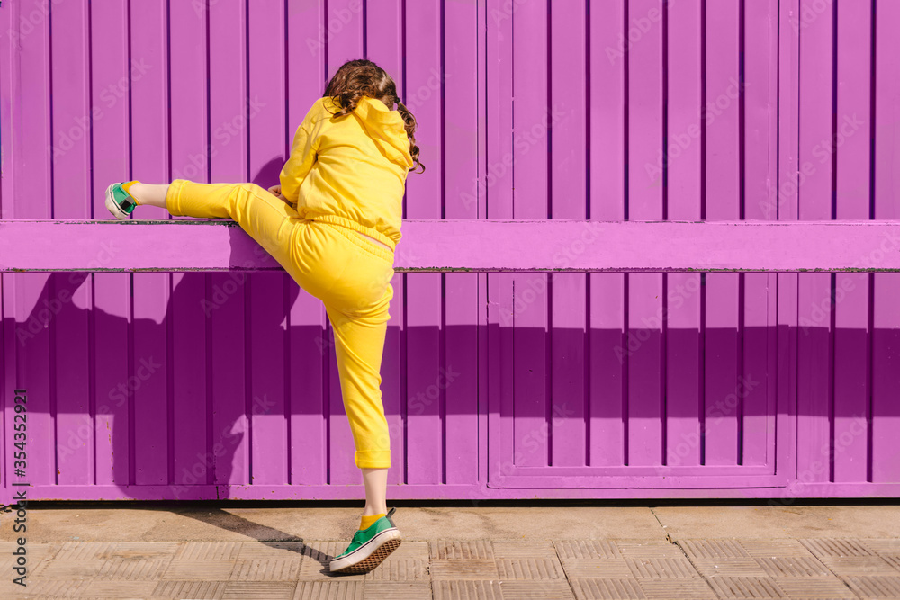 Back view of girl dressed in yellow climbing on bar in front of purple ...