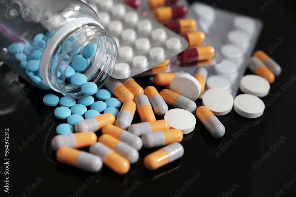 Pills on a dark glass table, different medication in capsules and ...
