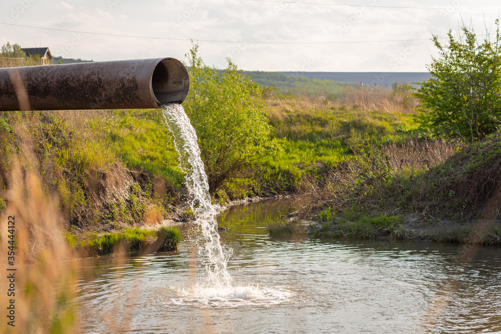 water flows from a pipe into a river against the backdrop of nature ...