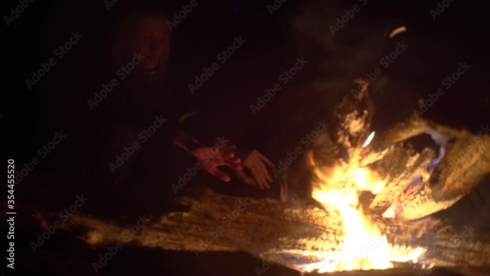 Friends sit by the fire at night. Bonfire around people, basking in the ...