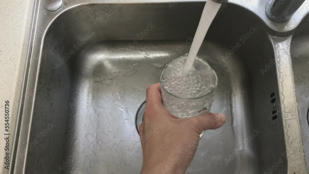 Man wash the glass cup in the stainless sink with the water running ...