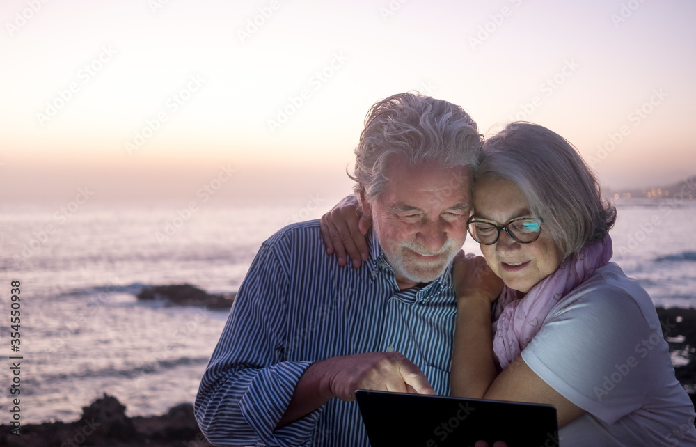 Happy retired couple having fun sitting on the cliffs, dusk light ...