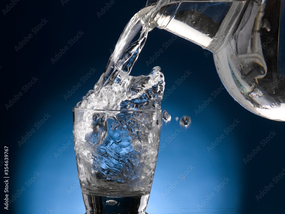Overflowing and spashing out glass of water. Blue background Stock ...