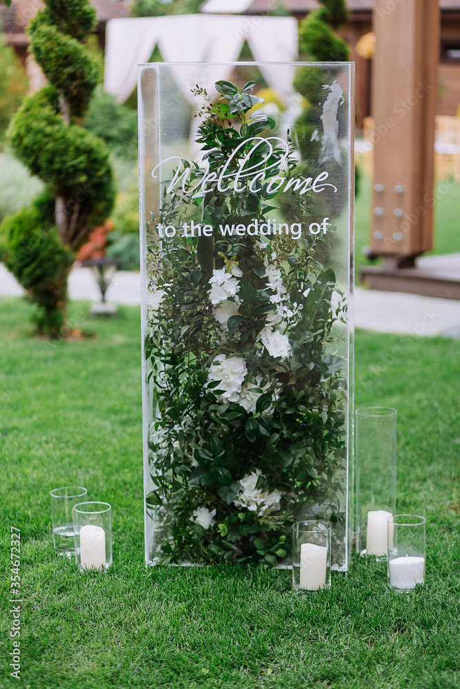 Welcome to the wedding of glass sign stand decorated with flowers and ...