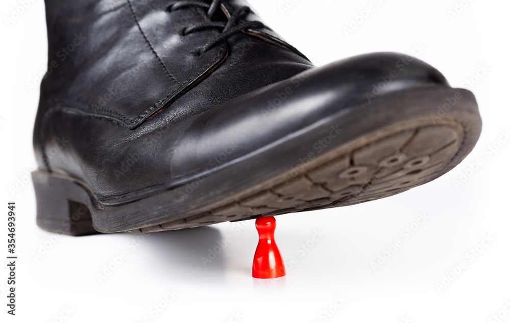 Black classy boot stomping and crushing a small red pawn game piece ...