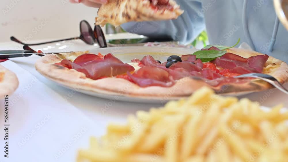 A man eats pizza with prosciutto, mozzarella, basil in a restaurant ...