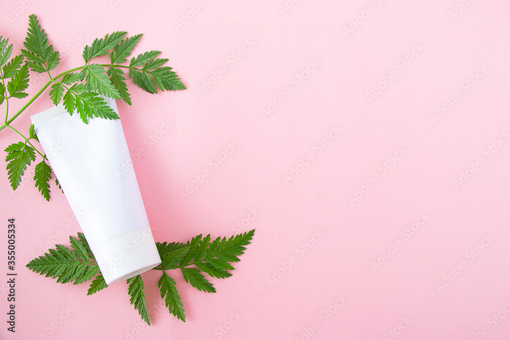 Cosmetic container with green herbal leaves on a pastel pink background ...