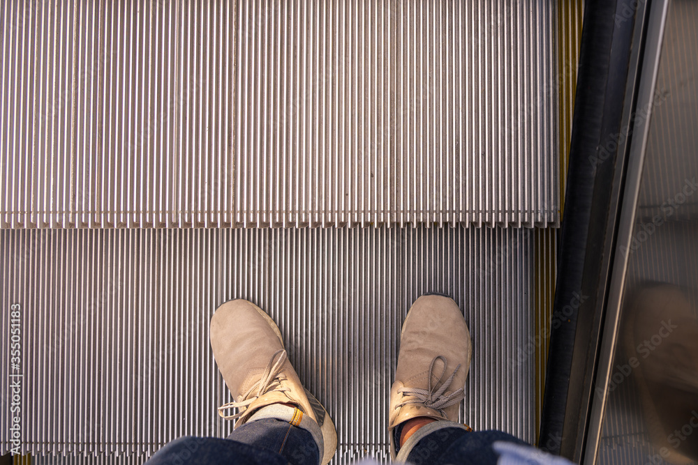 Top view, Feet wear Suede leather sneaker stand on tread of escalator ...