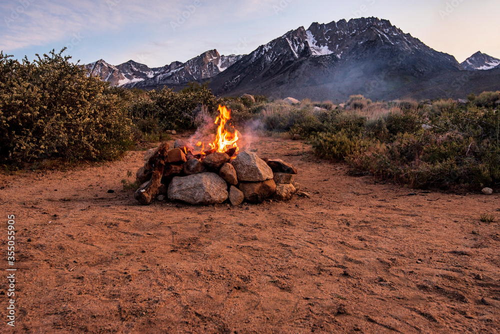 campfire in stone fire pit in desert at base of mountains with sunset ...