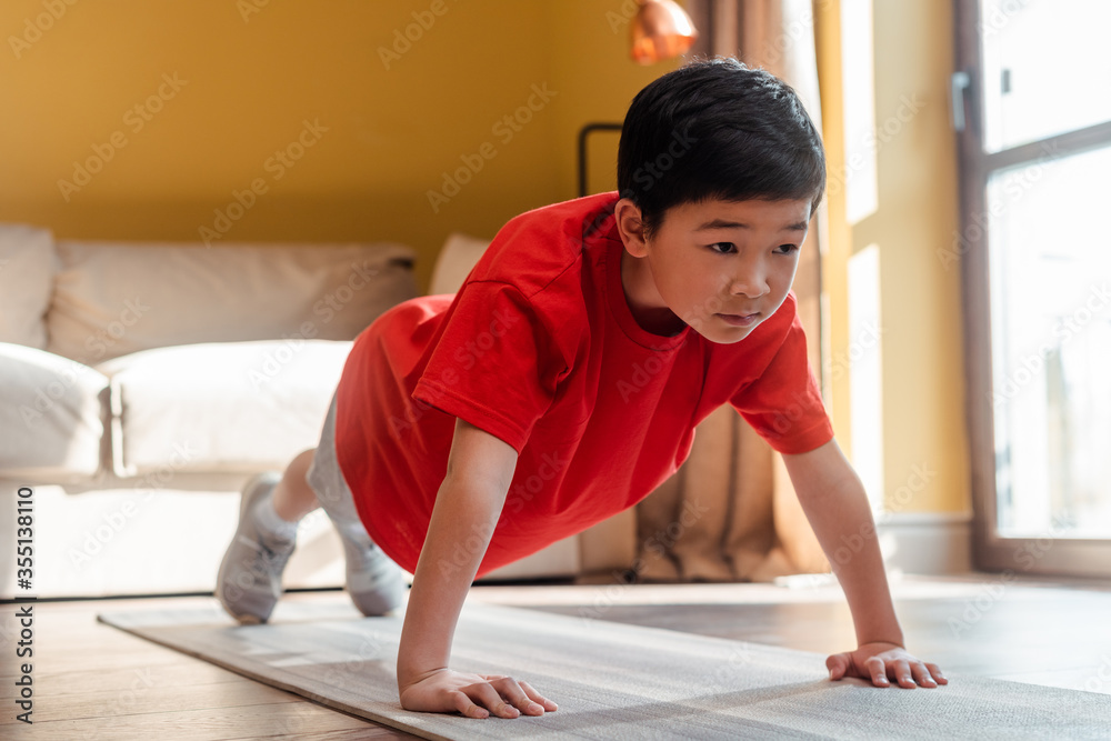 sportive asian kid doing push ups on fitness mat at home during self ...