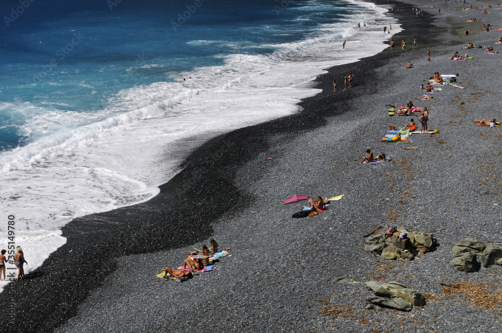 Foto de plage de galet noir en contraste avec les vacanciers colorés et ...