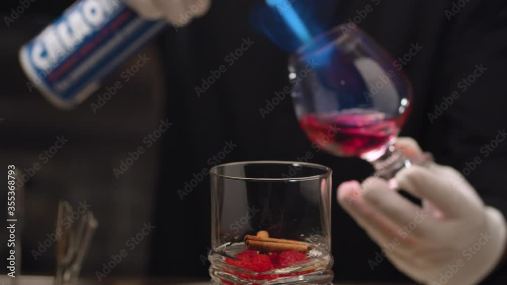 Making of Raspberry Sambuca. Close up barmans hand sets fire to sambuca ...