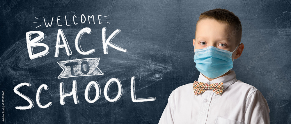 School boy wearing face mask standing against blackboard. Safe back to ...