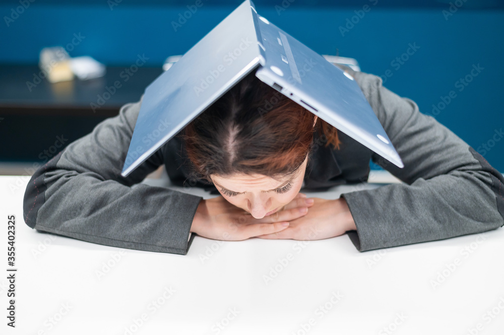 Problems at work. An exhausted woman folded her laptop over her head at ...