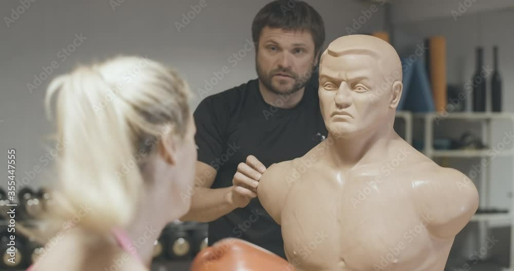 Back view of blond female boxer punching mannequin with blurred ...