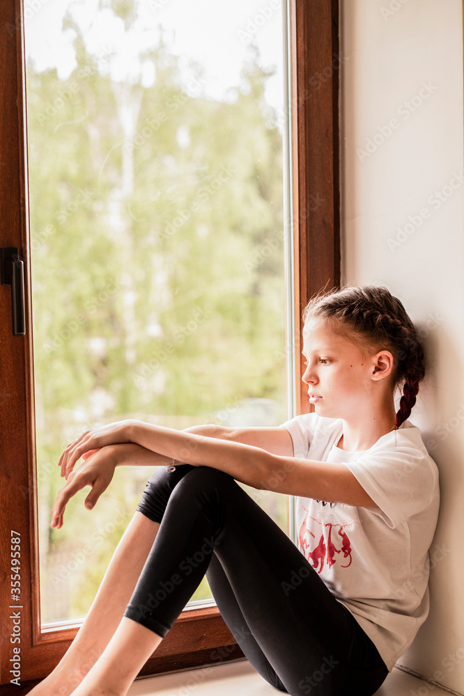A Teenage Girl Sits On A White Window Sill By The Window In The House