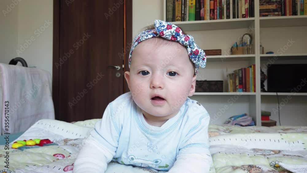 Cute baby girl with hairband (ribbon) lying on her tummy on bed. Cute ...