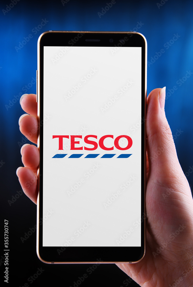 Hands holding smartphone displaying logo of Tesco Stock Photo | Adobe Stock