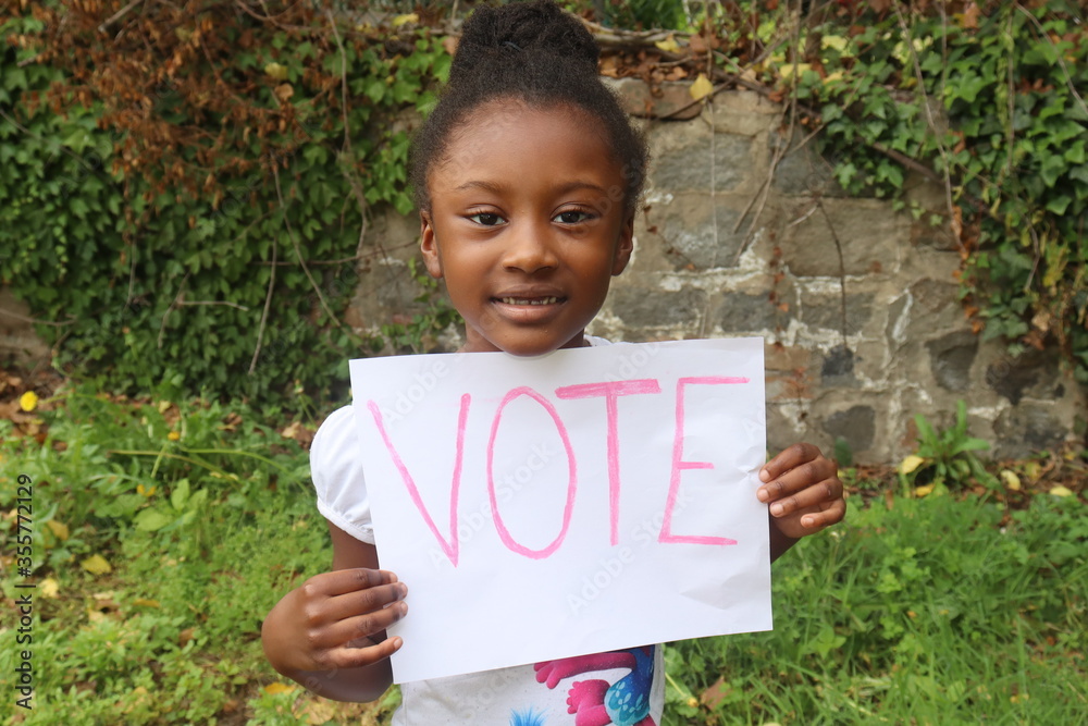 Young child holding white paper sign with word Vote written in Pink ...