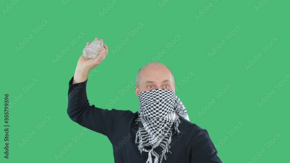 Anarchist protestor in checkered bandana swings stone on green screen ...