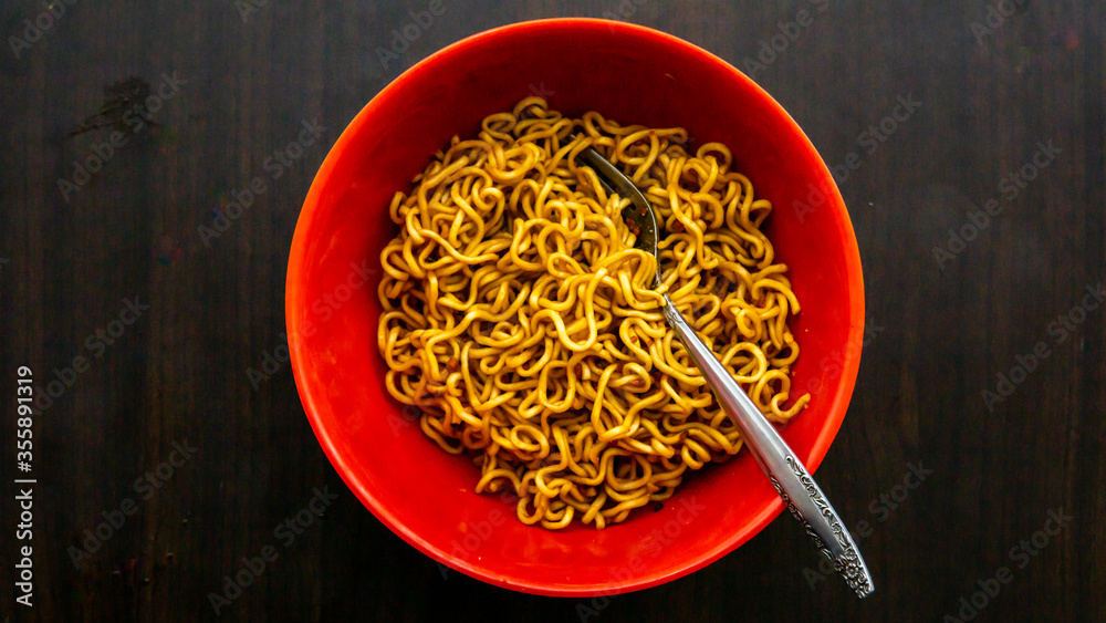 Top view of fried instant noodle or maggie with fork in a red bowl with ...