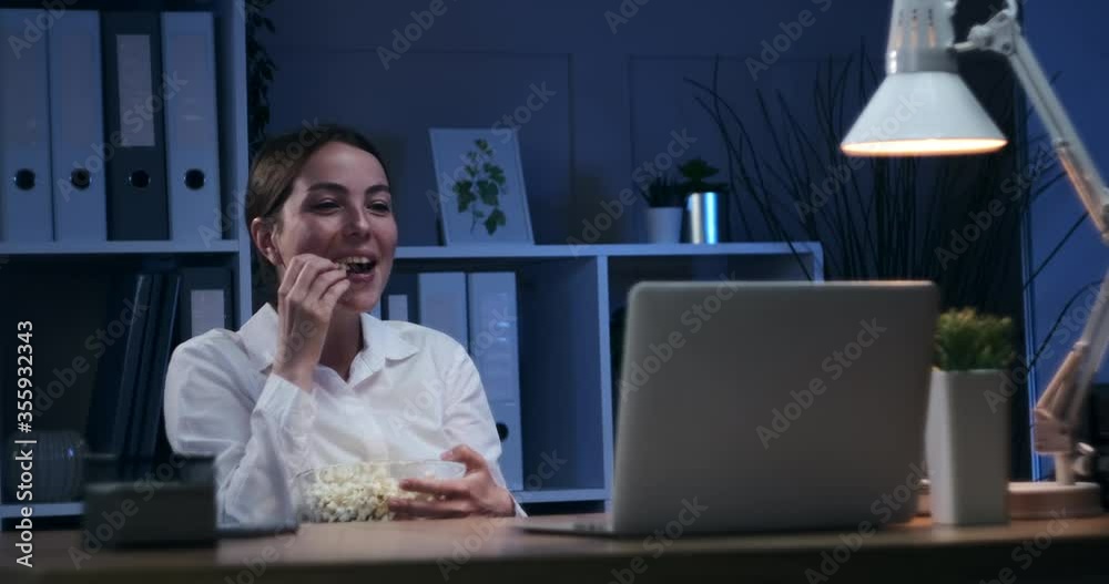 Businesswoman having fun eating popcorn and watching movie on office ...