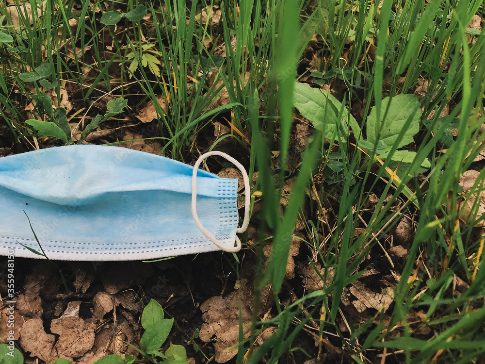 Disposable dirty face mask on ground, single use plastic trash on grass ...