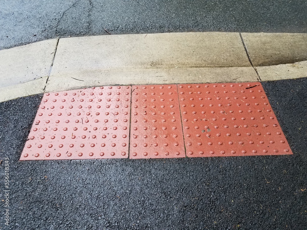 wet red tactile bumps on sidewalk with asphalt Stock Photo | Adobe Stock