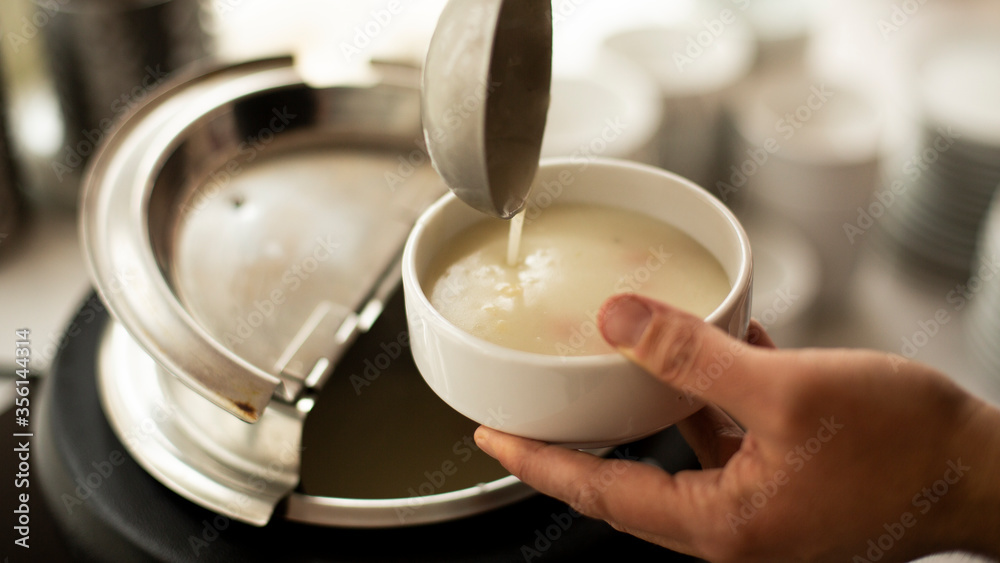 a mans hand holds a ladle and puts on the soup ,A man pouring soup into ...