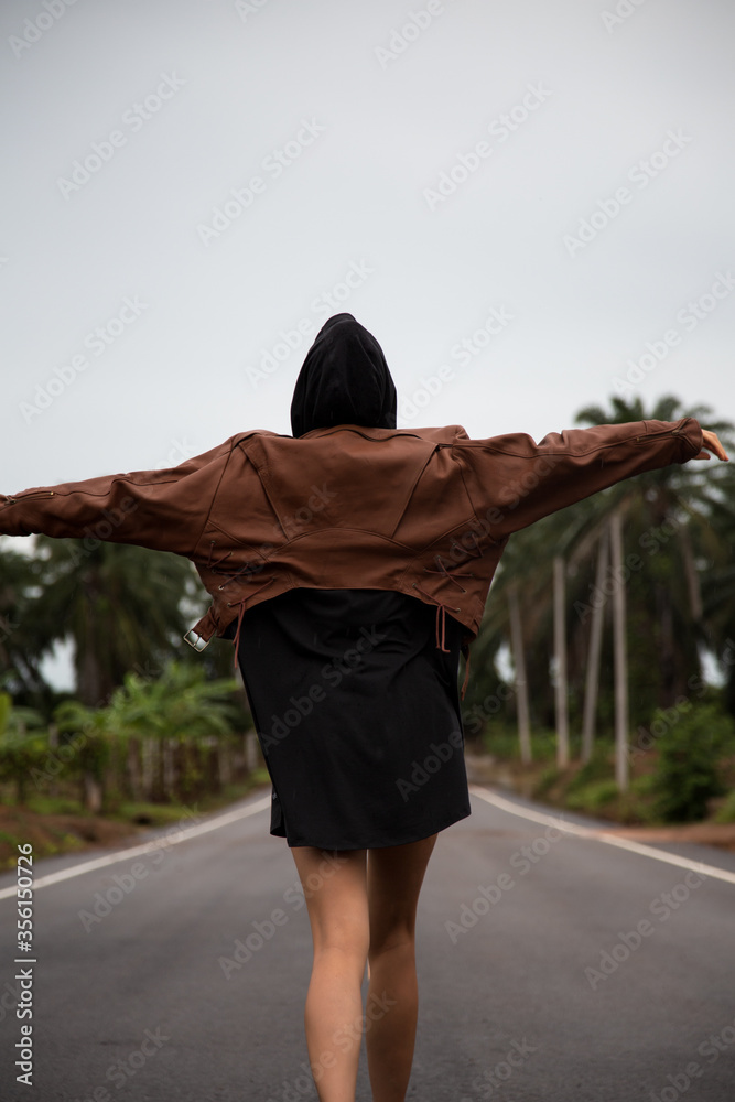 Girl in a brown leather jacket is on a paved road with a yellow stripe ...