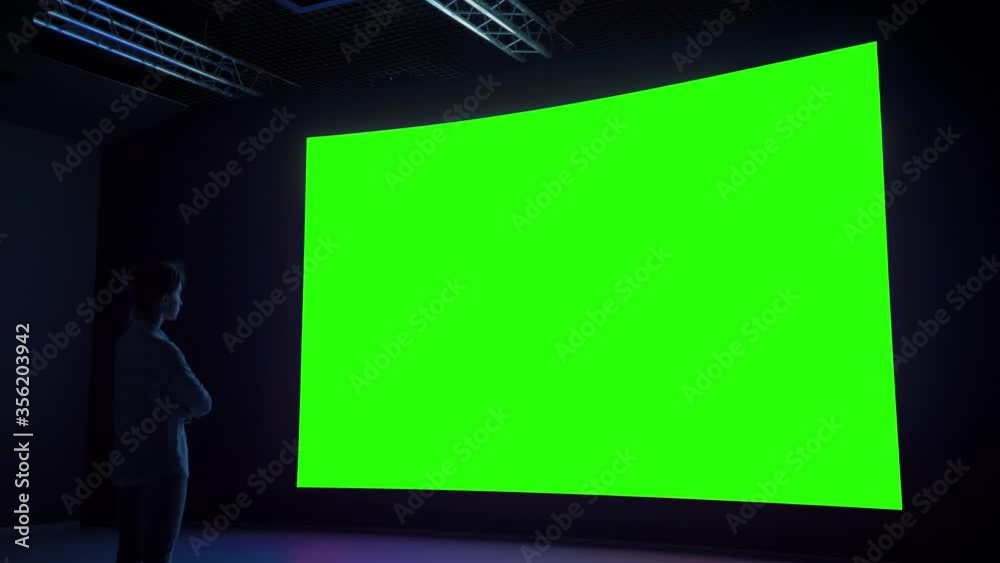 Woman looking at large wall blank interactive green display in dark ...