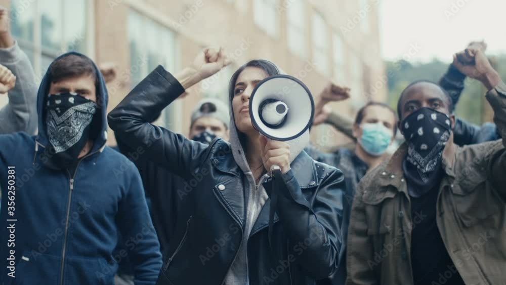 Caucasian young woman in hood screaming mottos in megaphone. Mixed ...