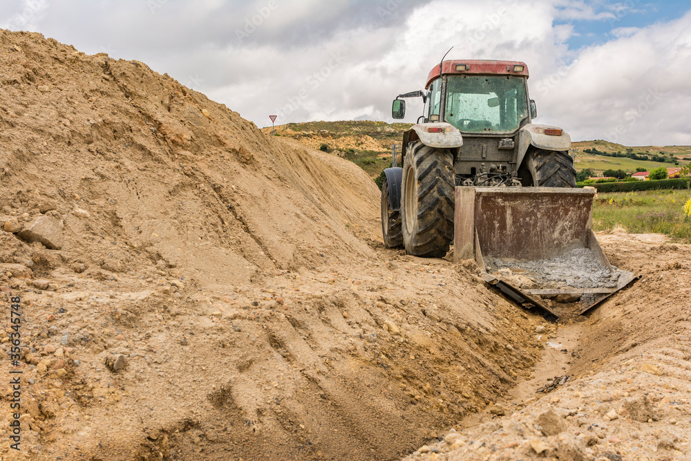 Tractor constructing a water pipeline ditch at road construction works ...