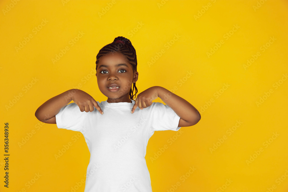 Pointing at herself. Little african-american girl's portrait on yellow ...