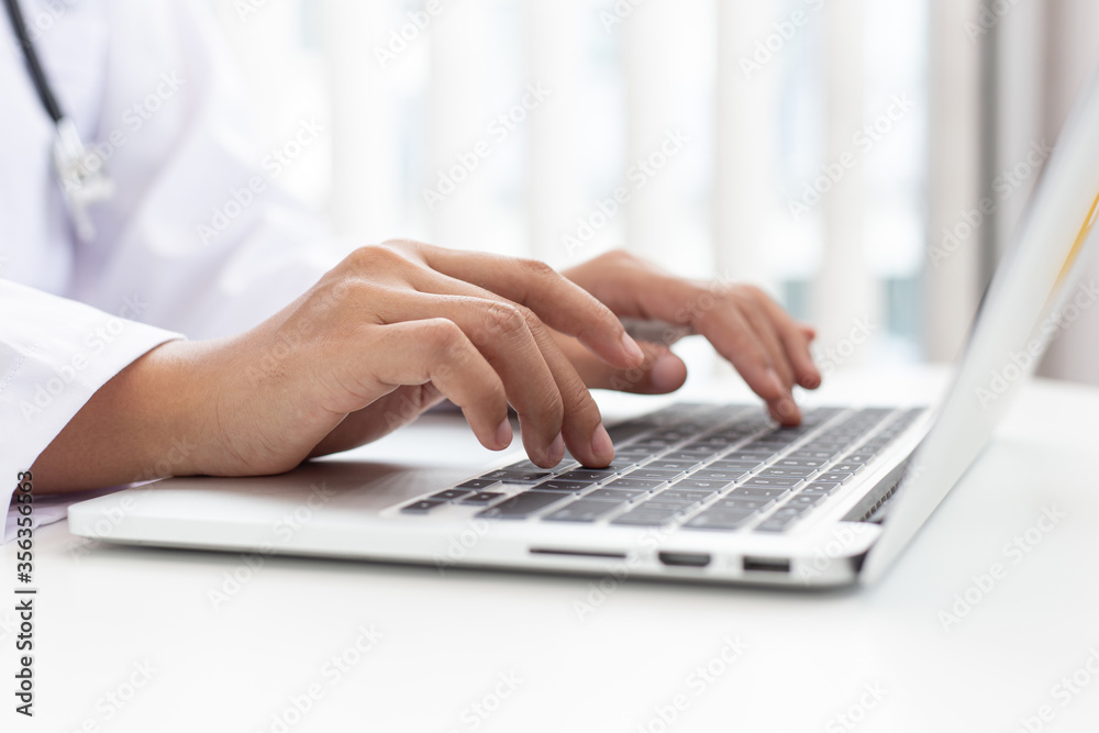 Doctor uses a laptop computer to record patient information and write ...
