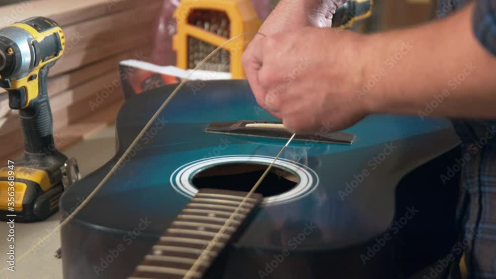 A man restoring a blue guitar grabs a new string and string knob and ...