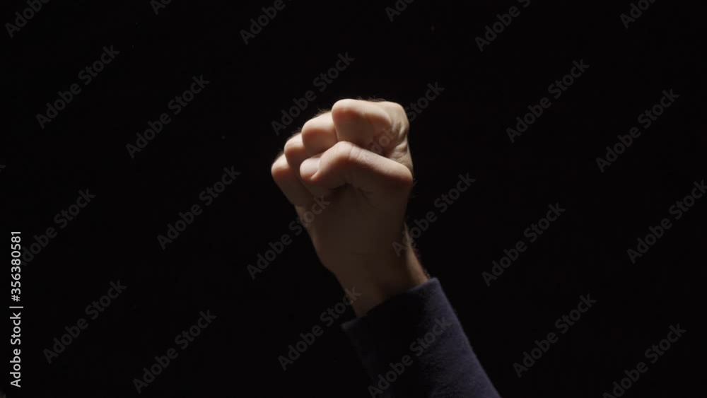 Clenched fist hand raises up in air on black background - sign of ...