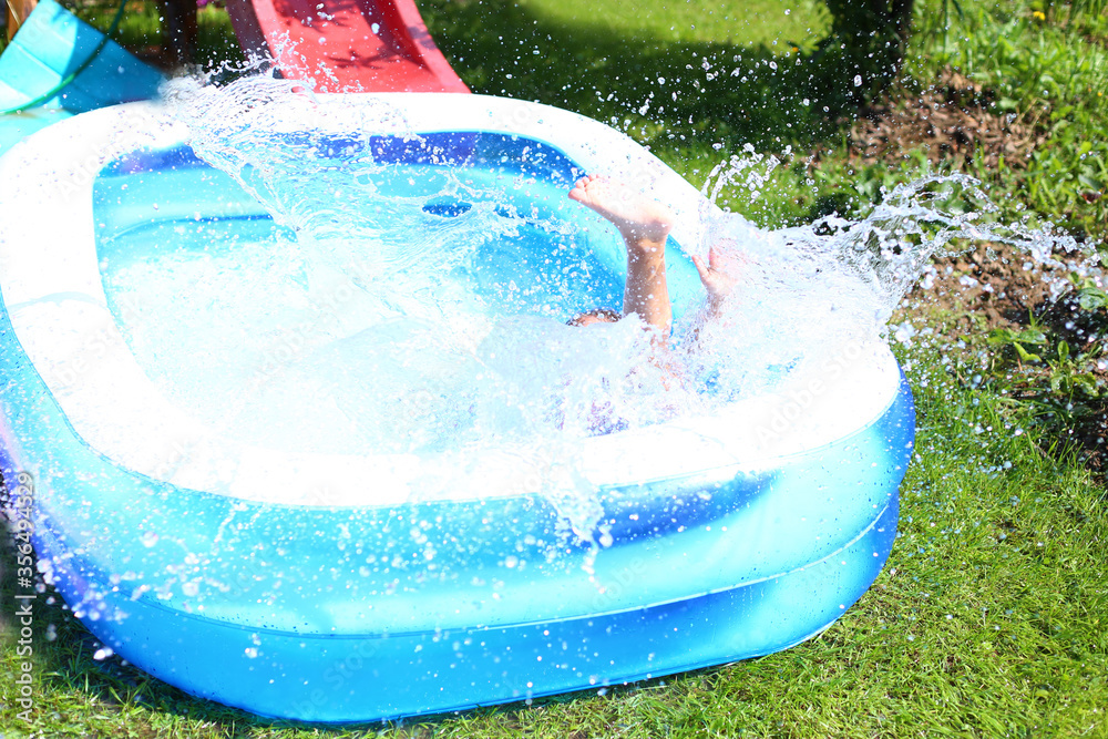 Staycation at home. Little girl in swimsuit rolls down slide into ...