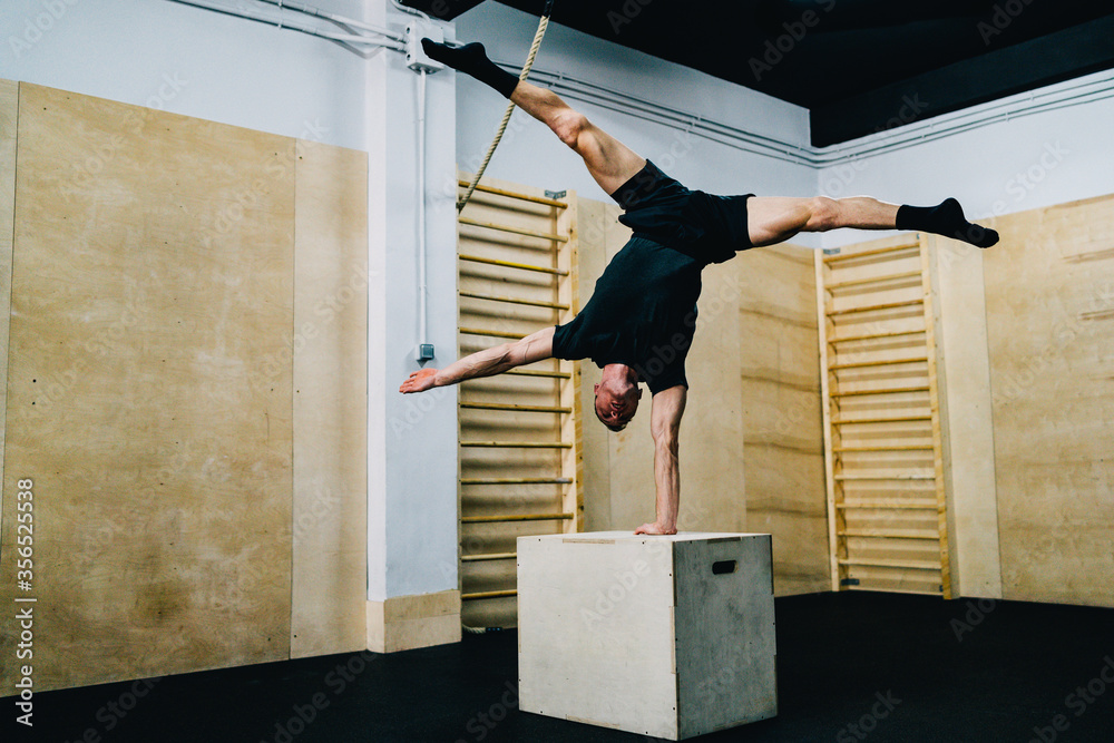 Flexible male gymnast in active wear performing acrobatic element in ...