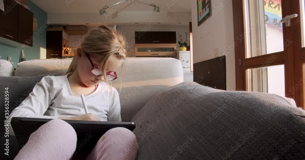 kid using tablet at home sitting on the couch. Little girl sitting on ...