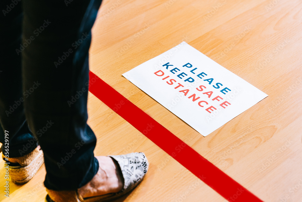 Please keep safe distance. Woman waiting behind a red line to enter a ...
