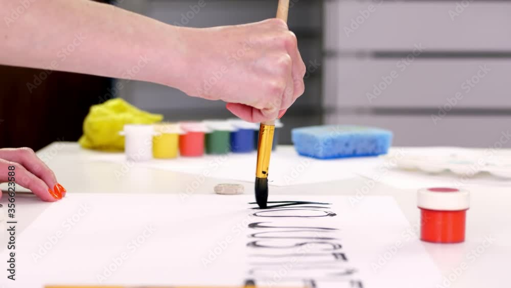 close-up, hand writes slogan with brush, using black watercolor paint ...