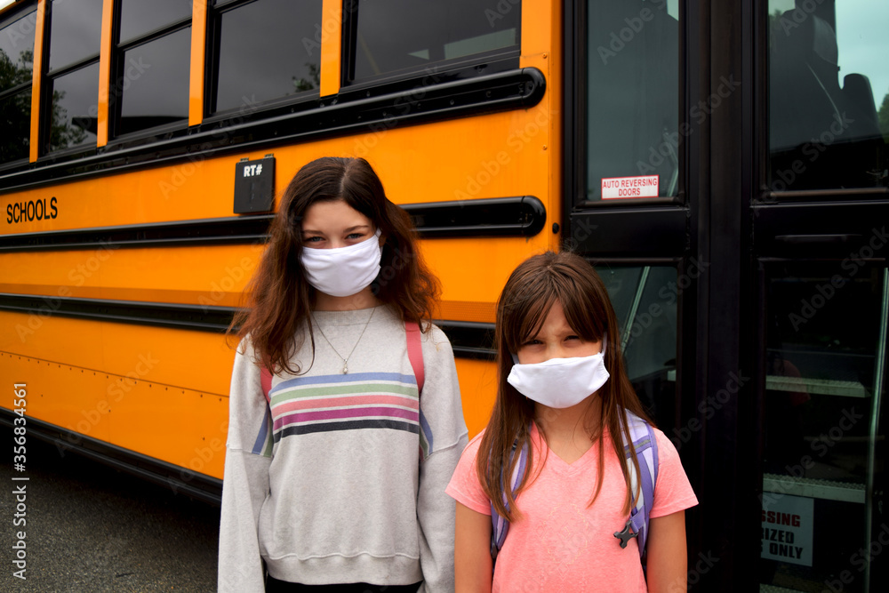 Children wearing face masks by school bus. Two girls wear facemasks ...