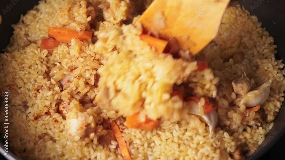 cooking pilaf close-up. Cook mixing rice, garlic pork and sliced carrot ...