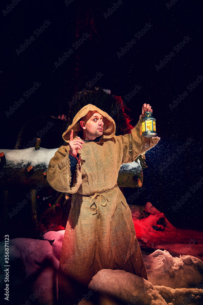 Medieval monk in canvas sackcloth robe with lattern in dark forest with ...