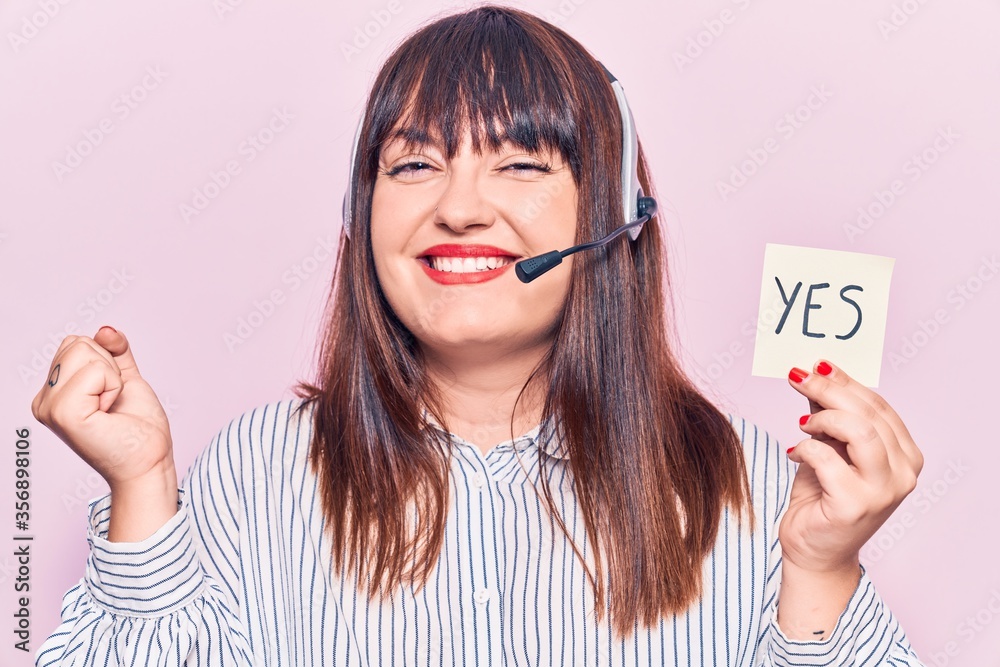 Young plus size woman wearing call center agent headset holding yes ...