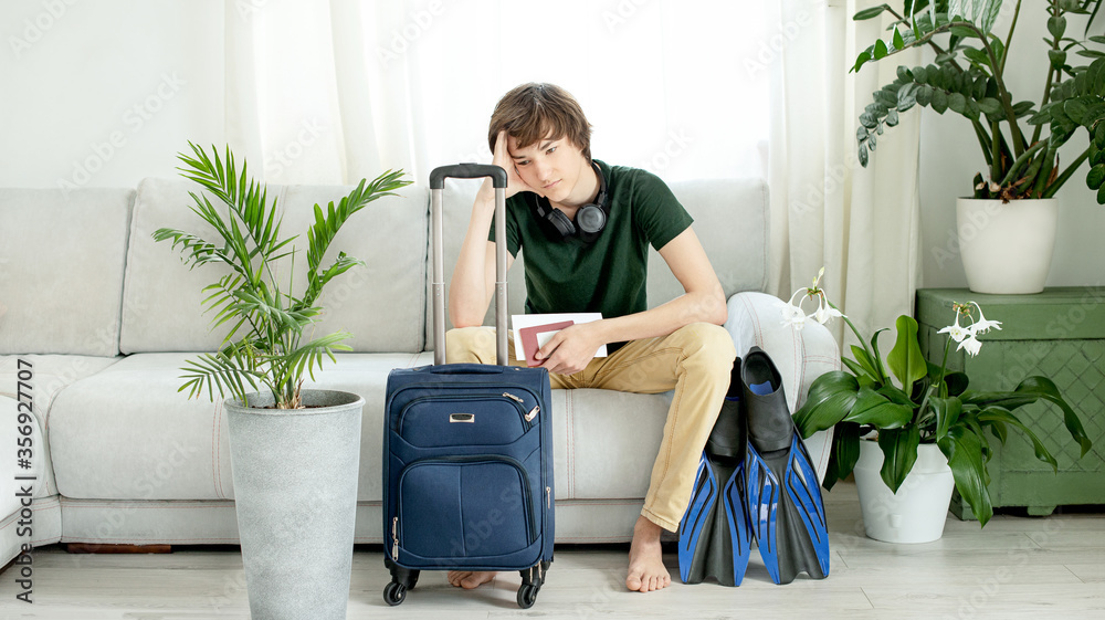 Sad tourist teen with a suitcase and flippers stays at home during the ...