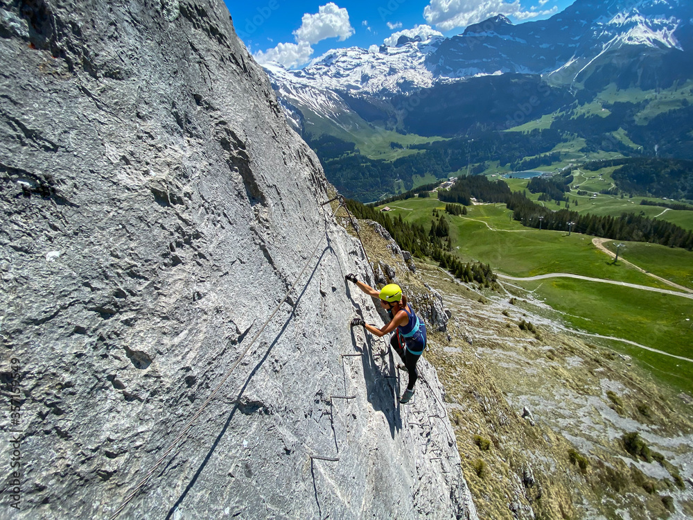 Pretty female climber on a steep Via Ferrata in the Swiss Alps ...