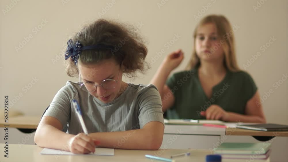 A girl from the back desk distracts her classmate. Schoolgirl is angry ...
